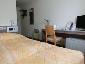 Quarto de hotel com cama, escrivaninha com cadeira, televisão, micro-ondas e um pequeno frigorífico.