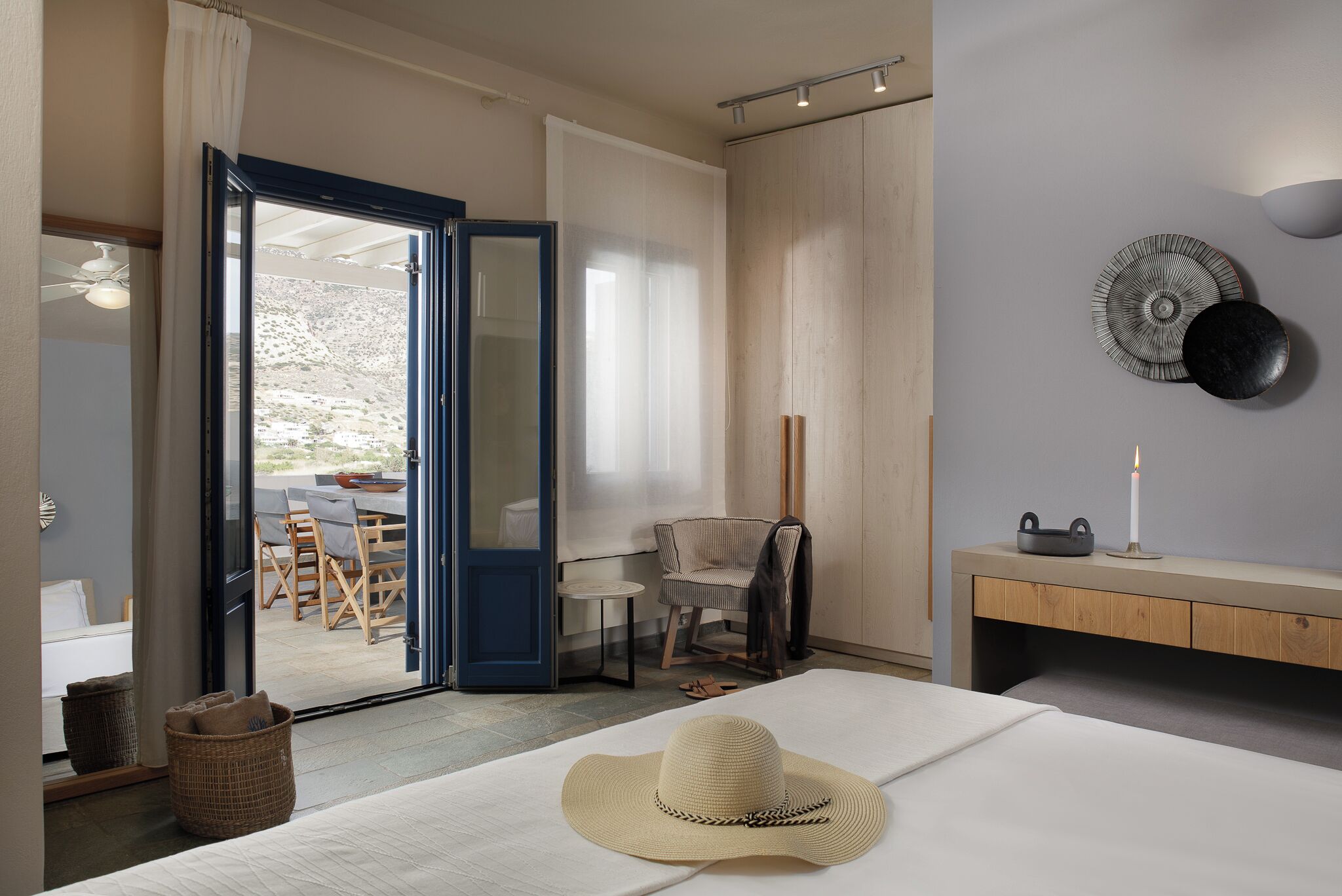 Quarto com cama, cadeira, mesa e porta que dá para uma área externa.