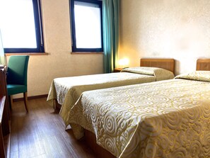 Quarto de hotel com duas camas de solteiro, uma escrivaninha e uma cadeira.