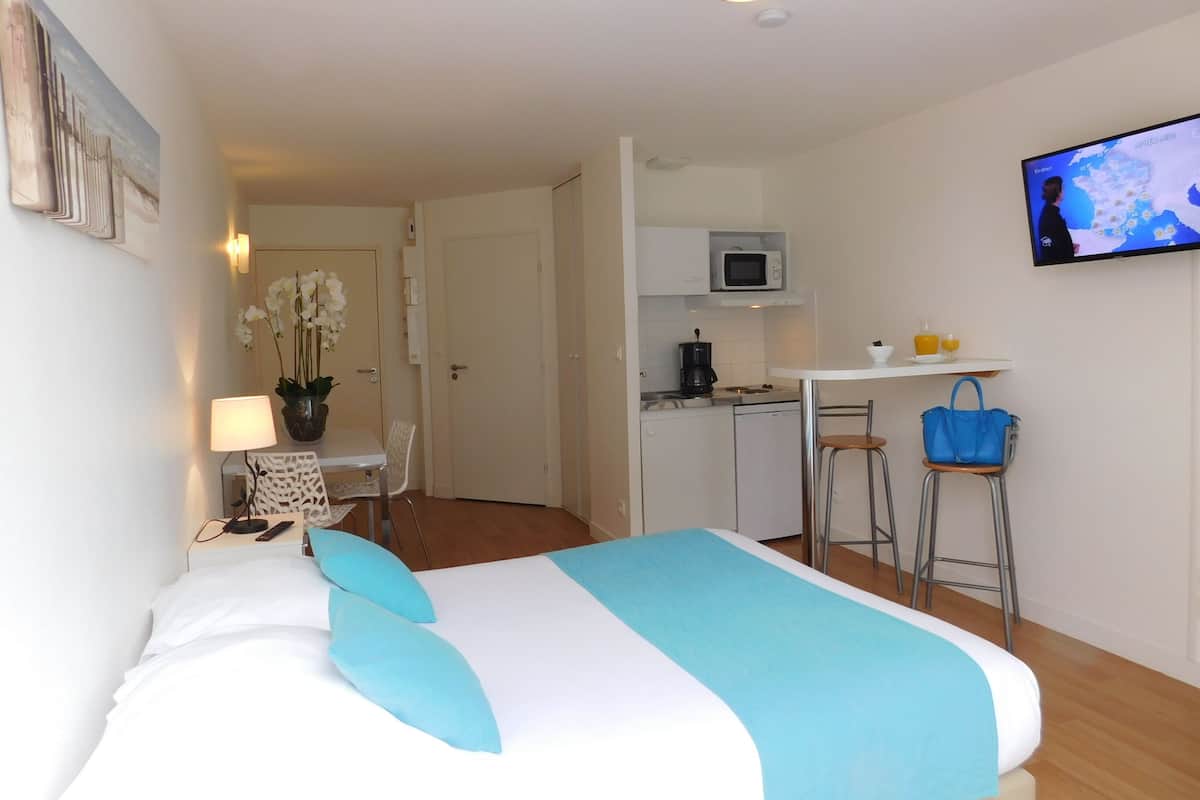 Quarto de hotel com cama, escrivaninha com cadeira, micro-ondas e televisão.