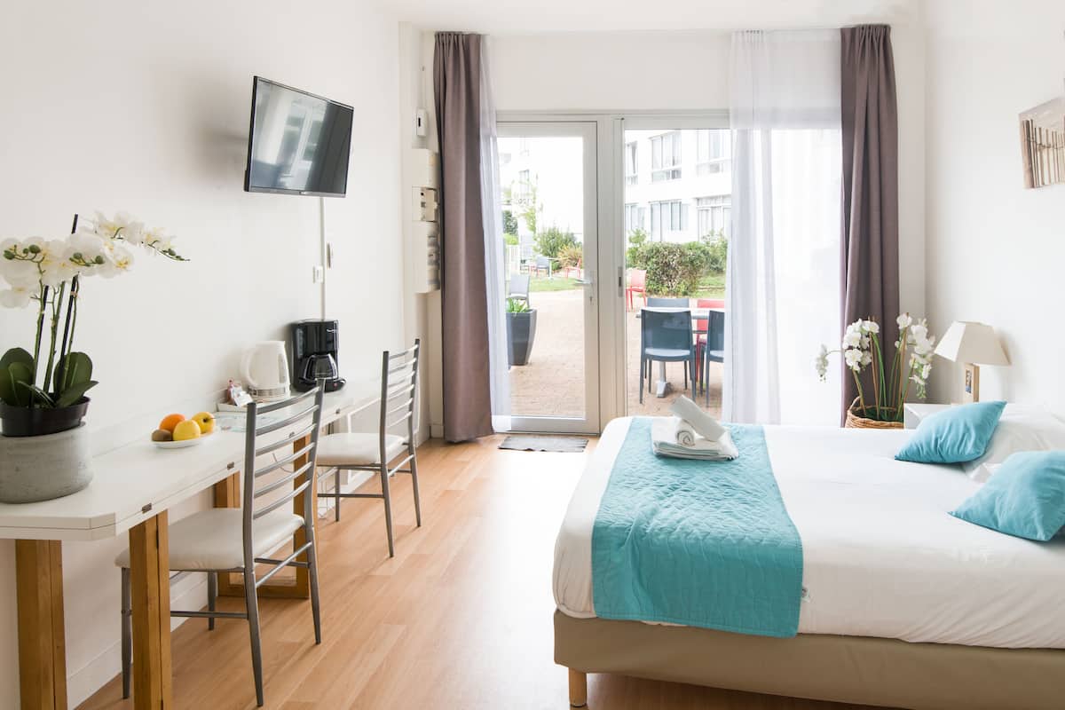 Quarto de hotel com cama, escrivaninha com cadeira, televisão e vista para o exterior.