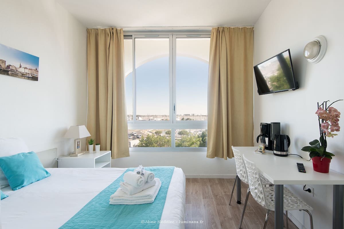 Quarto de hotel com cama, escrivaninha, televisão e vista para a cidade.