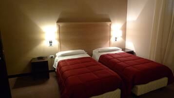 Quarto de hotel com duas camas, cada uma com um cobertor vermelho, cabeceira de madeira e luminárias de cabeceira.