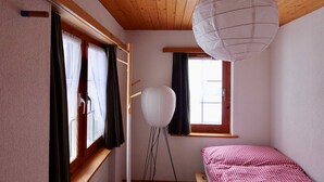 Quarto com teto de madeira, janela com cortinas, mesa de cabeceira e um lanterna de papel pendurada.