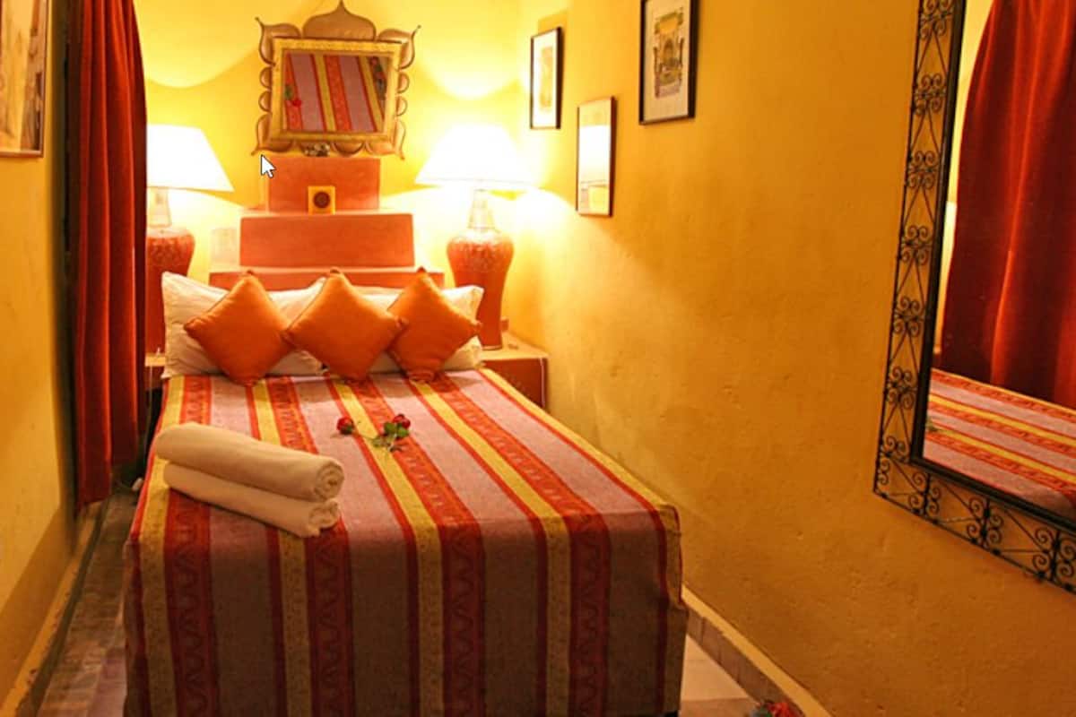 Quarto de hotel com uma cama, duas luminárias de cabeceira, um espelho e uma cortina vermelha.