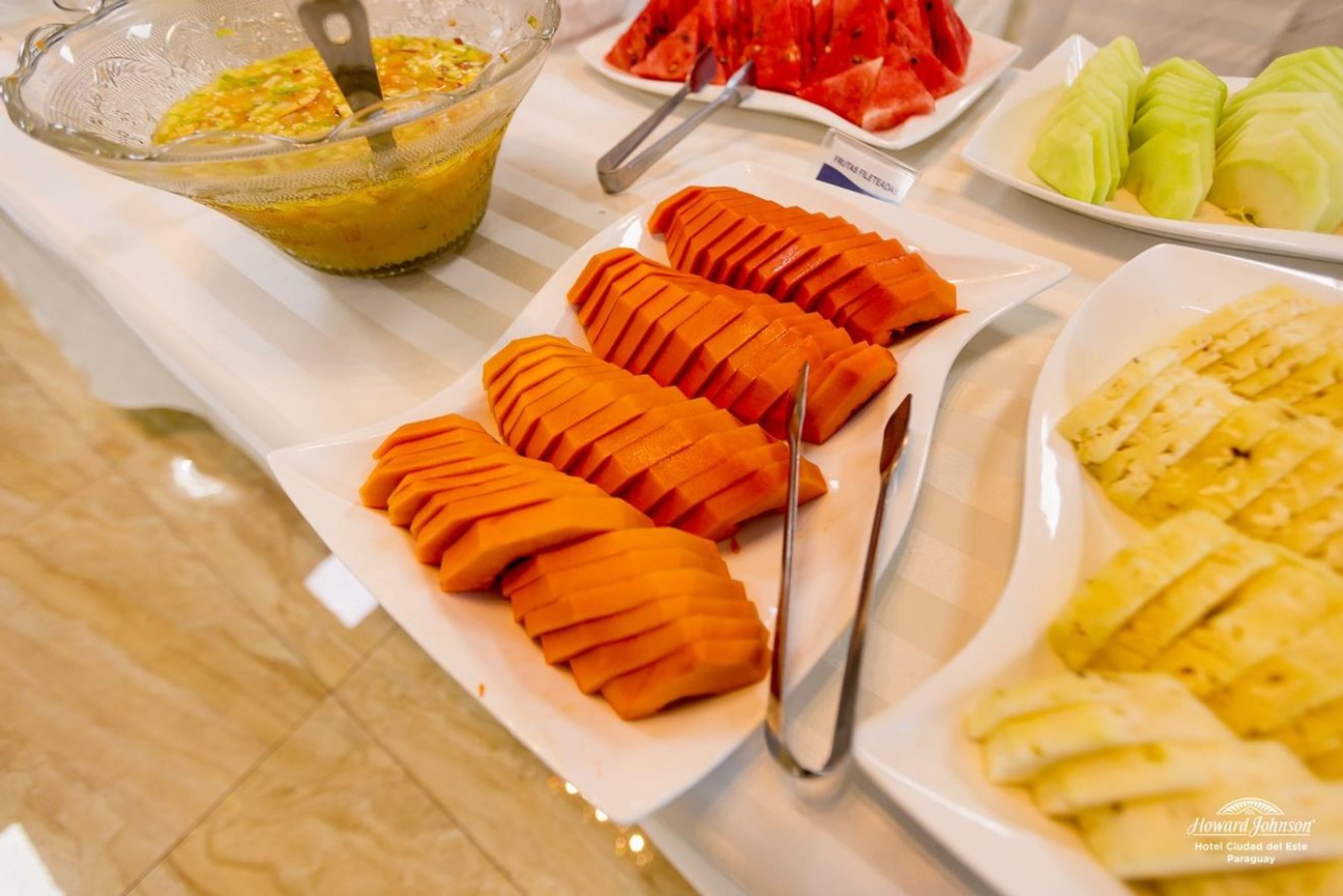 Buffet com mangas fatiadas, melancia e uma saladeira de frutas.