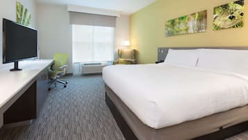 Quarto de hotel com uma cama grande, uma escrivaninha com computador, uma cadeira e uma janela com vista.