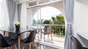 Uma varanda com mesa e cadeiras de vidro, um vaso de planta e vista para áreas verdes e edifícios.