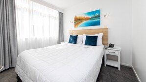 Quarto de hotel com uma cama grande, mesa de cabeceira com telefone e um quadro na parede.
