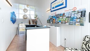 Uma área de recepção com balcão, um quadro com um veleiro e uma vitrine com folhetos.