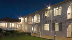 Um motel com estrutura em dois andares, janelas em arco e um gramado bem cuidado.