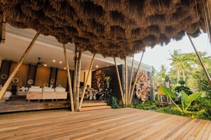 Um interior moderno com um deck de madeira, um telhado de palha e uma área de estar com sofás e uma mesa de jantar.
