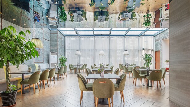 Uma sala de jantar moderna com piso de madeira, cadeiras estofadas em verde e uma mesa central.
