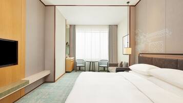Quarto de hotel com uma cama grande, televisão, escrivaninha com cadeira e uma mesinha.