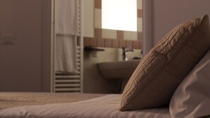 Quarto de hotel com cama, travesseiro, banheiro com pia e porta-toalhas.