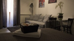 Quarto de hotel com uma cama, uma pequena mesa com cadeiras, um abajur, uma planta e obras de arte na parede.