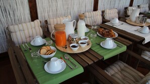 Disposição para o café da manhã com toalha de mesa verde, almofadas listradas e diversos itens como ovos, torradas e bebidas.