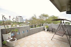 Varanda com cadeira de balanço, plantas em vasos e vista para edifícios e árvores.