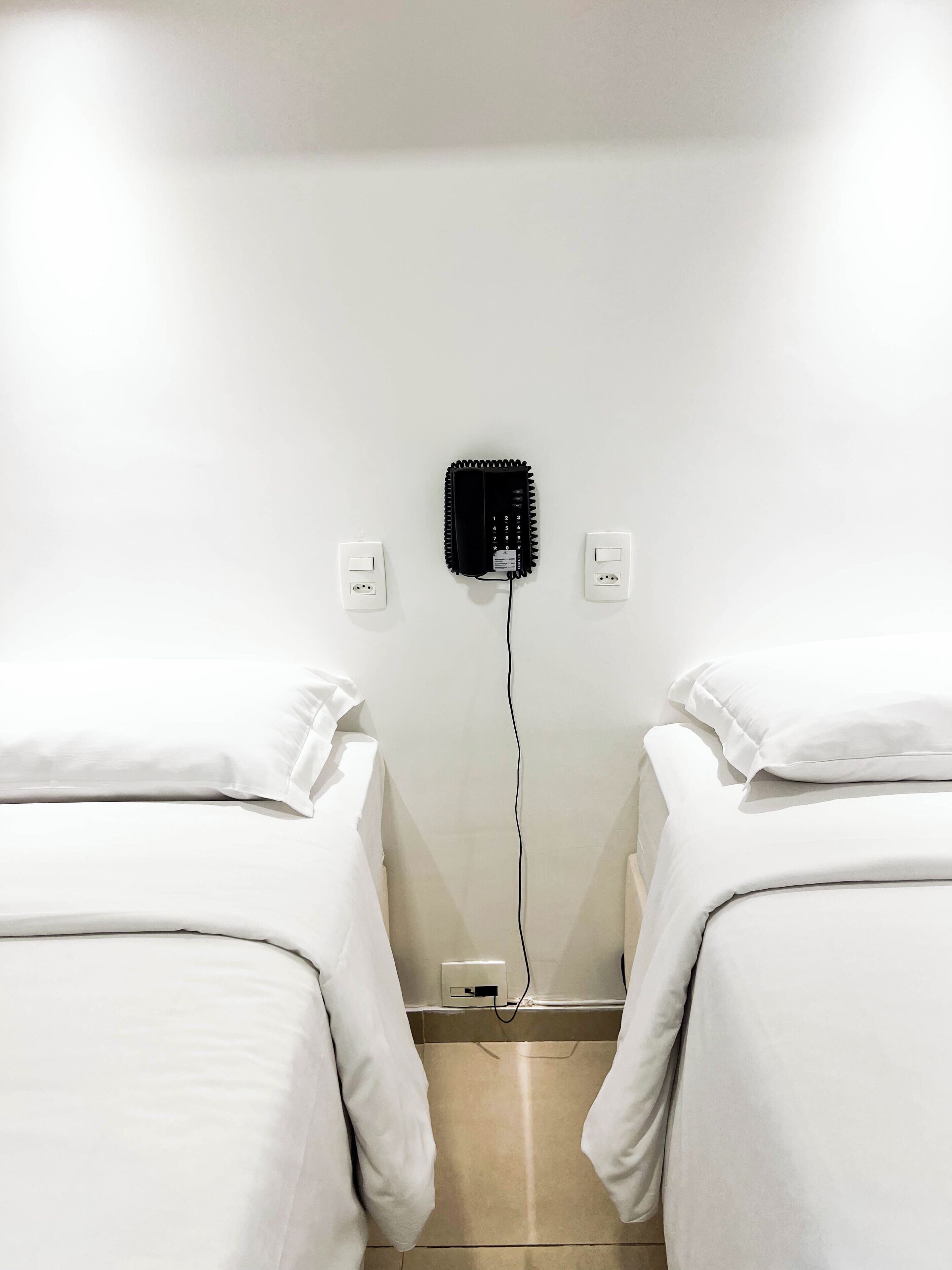 Quarto de hotel com duas camas, um secador de cabelo preto e uma tomada na parede.