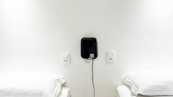 Quarto de hotel com duas camas, um secador de cabelo preto e uma tomada na parede.