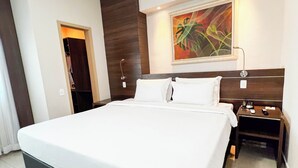 Quarto de hotel com cama grande, mesa de cabeceira, luminária na parede e um quadro.