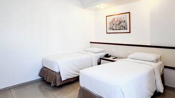Quarto de hotel com duas camas, uma mesa de cabeceira, um telefone e um quadro na parede.