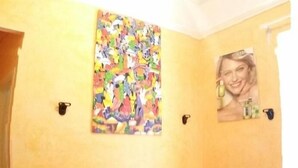 Quarto com cabeceira de madeira, colcha vermelha, mesinha de cabeceira com abajur e um quadro na parede.