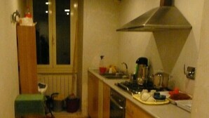 Cozinha compacta com armários de madeira, forno embutido e janela.