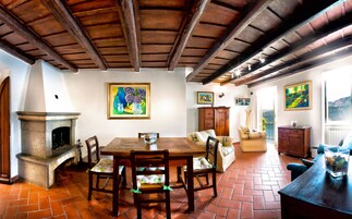 Uma área de jantar com lareira de pedra, vigas de madeira no teto e piso de azulejos.
