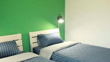 Quarto com duas camas, cada uma com roupa de cama listrada, uma parede verde e uma luminária de cabeceira.