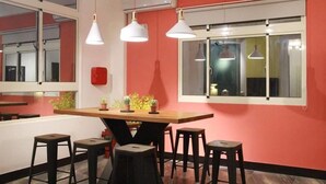 Uma cozinha moderna com mesa de madeira, banquetas, luminárias pendentes e uma parede com destaque em vermelho.