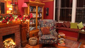 Uma sala de estar aconchegante com lareira, estante de livros, poltrona estampada e sofá com almofadas.