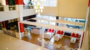 Amplo espaço interno com vários arranjos de assentos, uma mesa de recepção e um lustre.