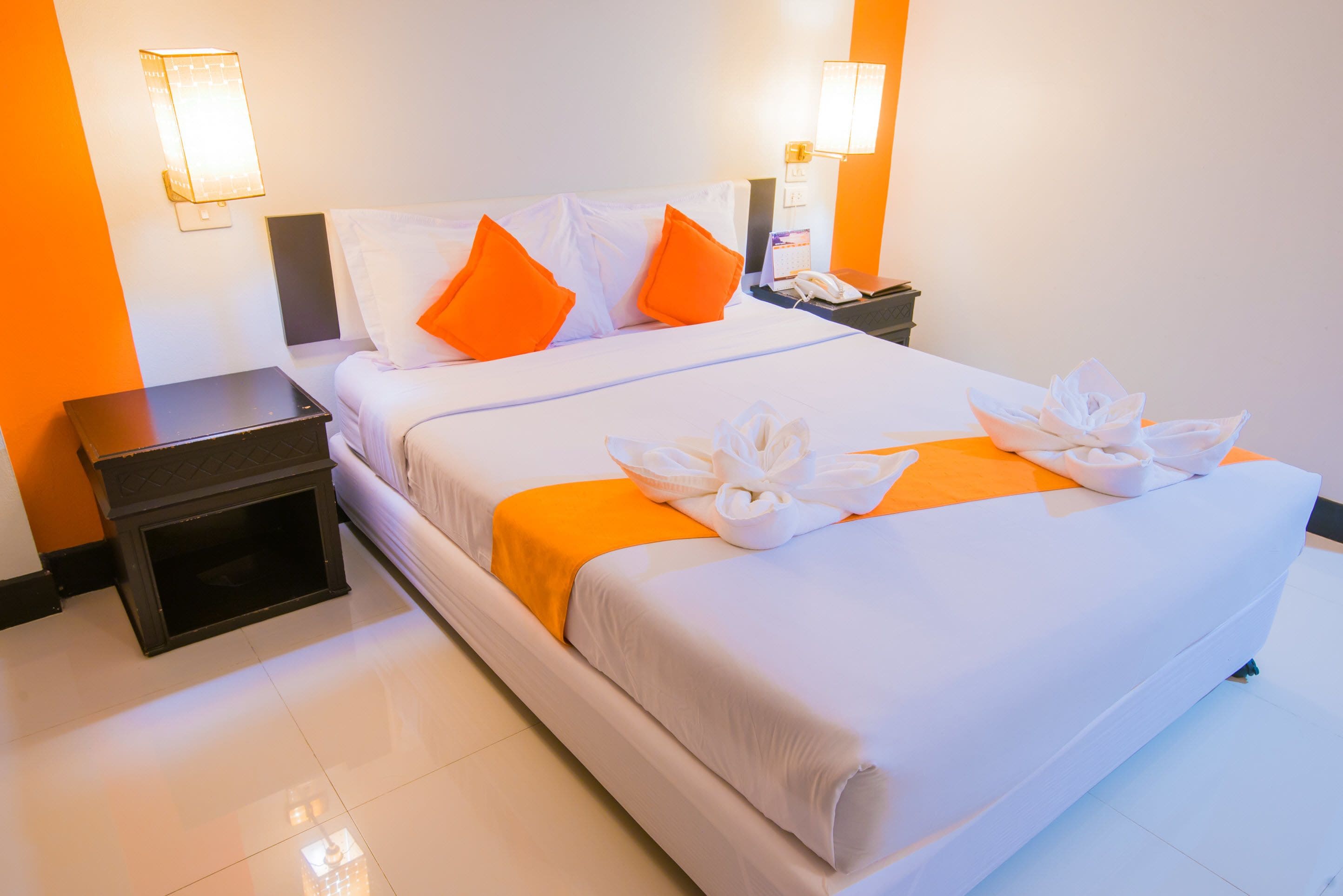 Quarto de hotel com uma cama grande, duas mesas de cabeceira e uma luminária fixada na parede.