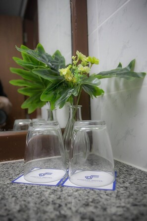 Dois vasos de vidro transparente com planta e flores sobre uma bancada de granito.
