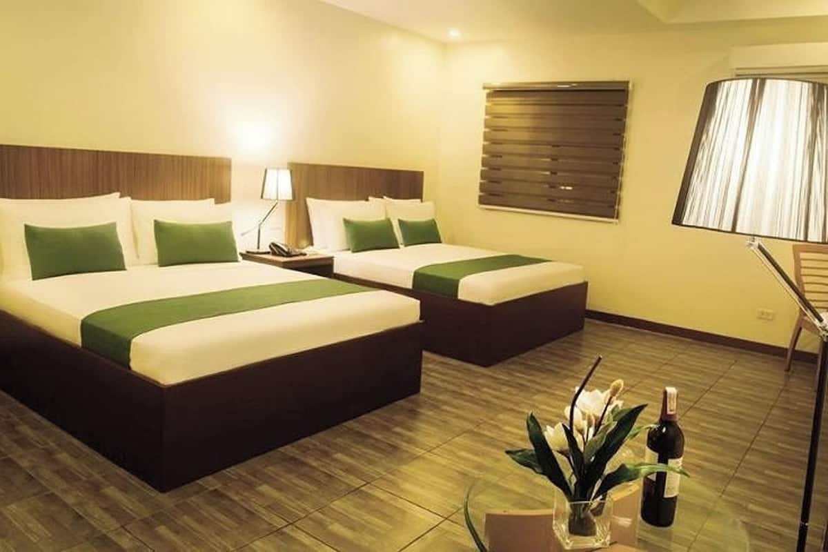Quarto de hotel com duas camas, uma mesa de cabeceira, uma luminária, uma janela com persianas e um vaso com flores.