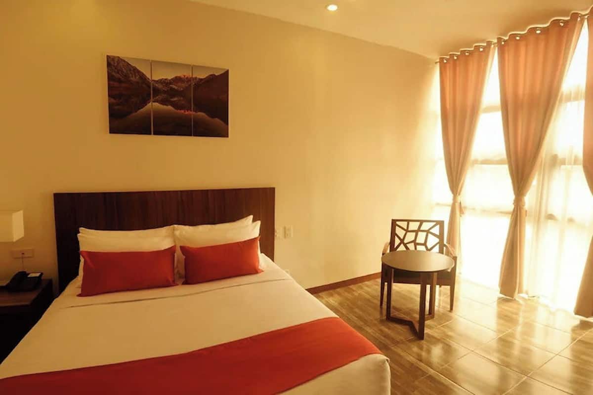 Quarto de hotel com uma cama grande, uma mesa pequena, uma cadeira e um quadro na parede.