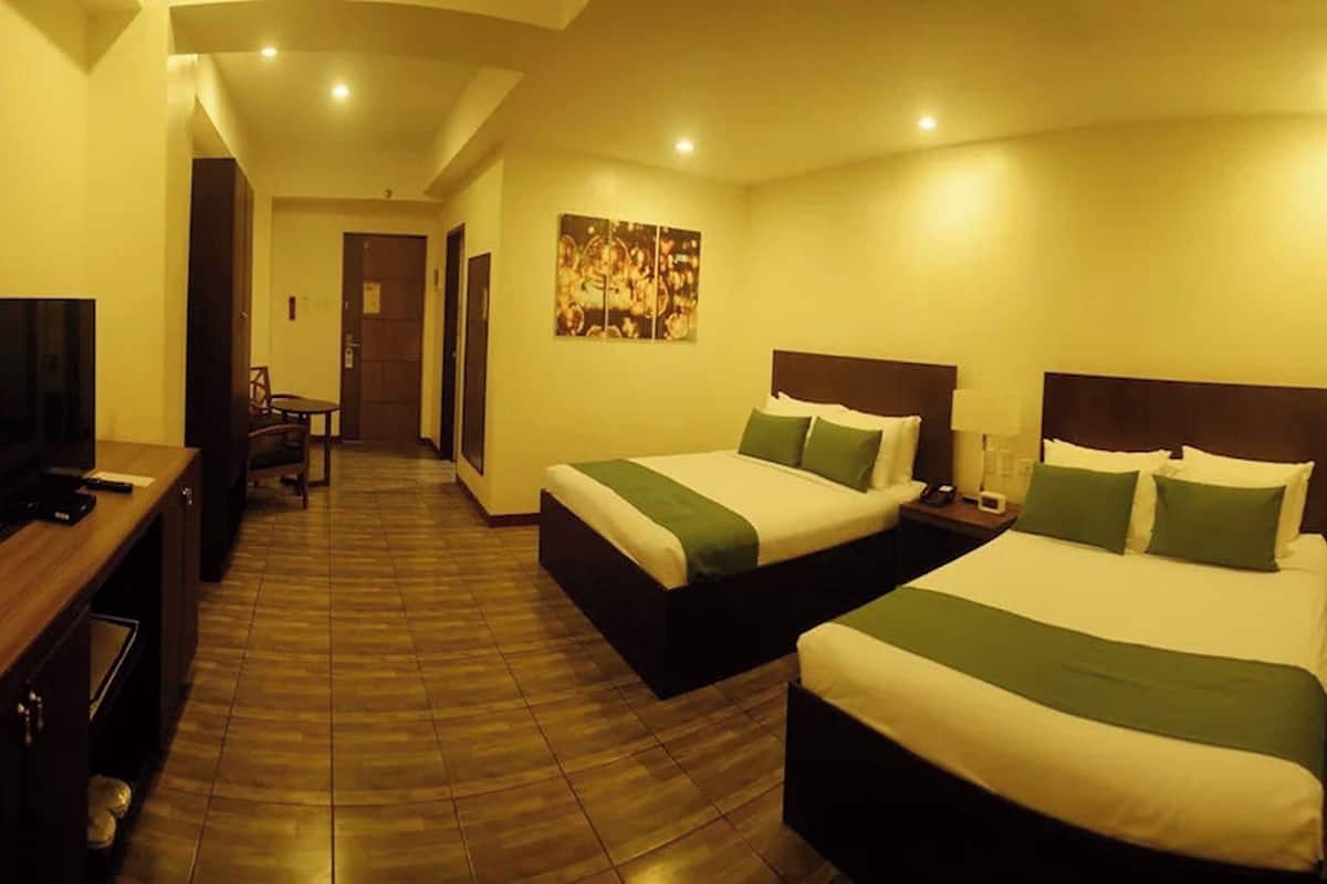 Quarto de hotel com duas camas, uma escrivaninha, uma cadeira e uma televisão.