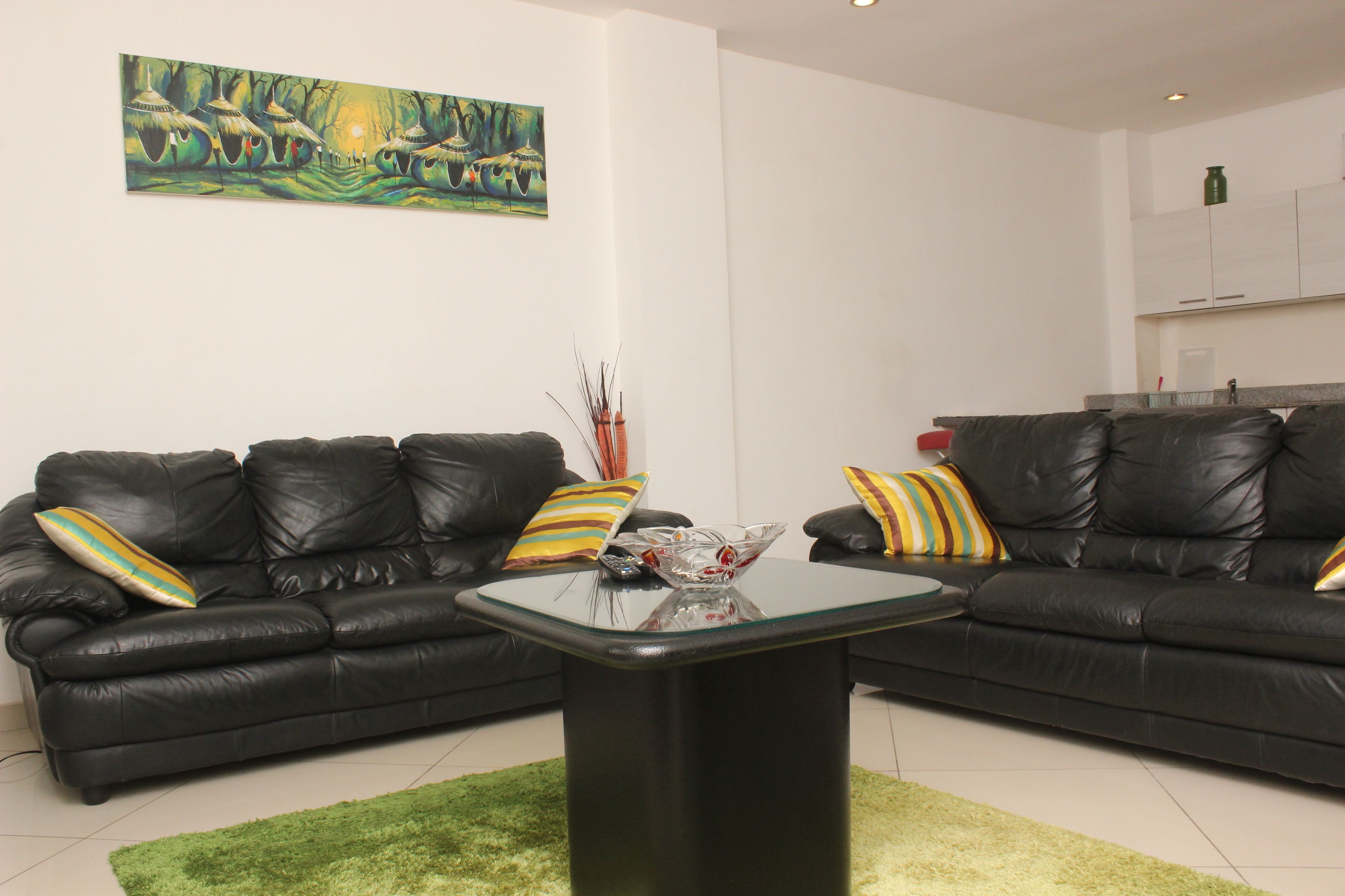 Sala de estar com dois sofás de couro preto, uma mesa de centro de vidro e um tapete verde.