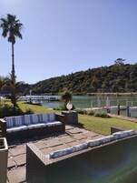 Um pátio com área de estar ao ar livre, piscina e vista para um lago e colinas.