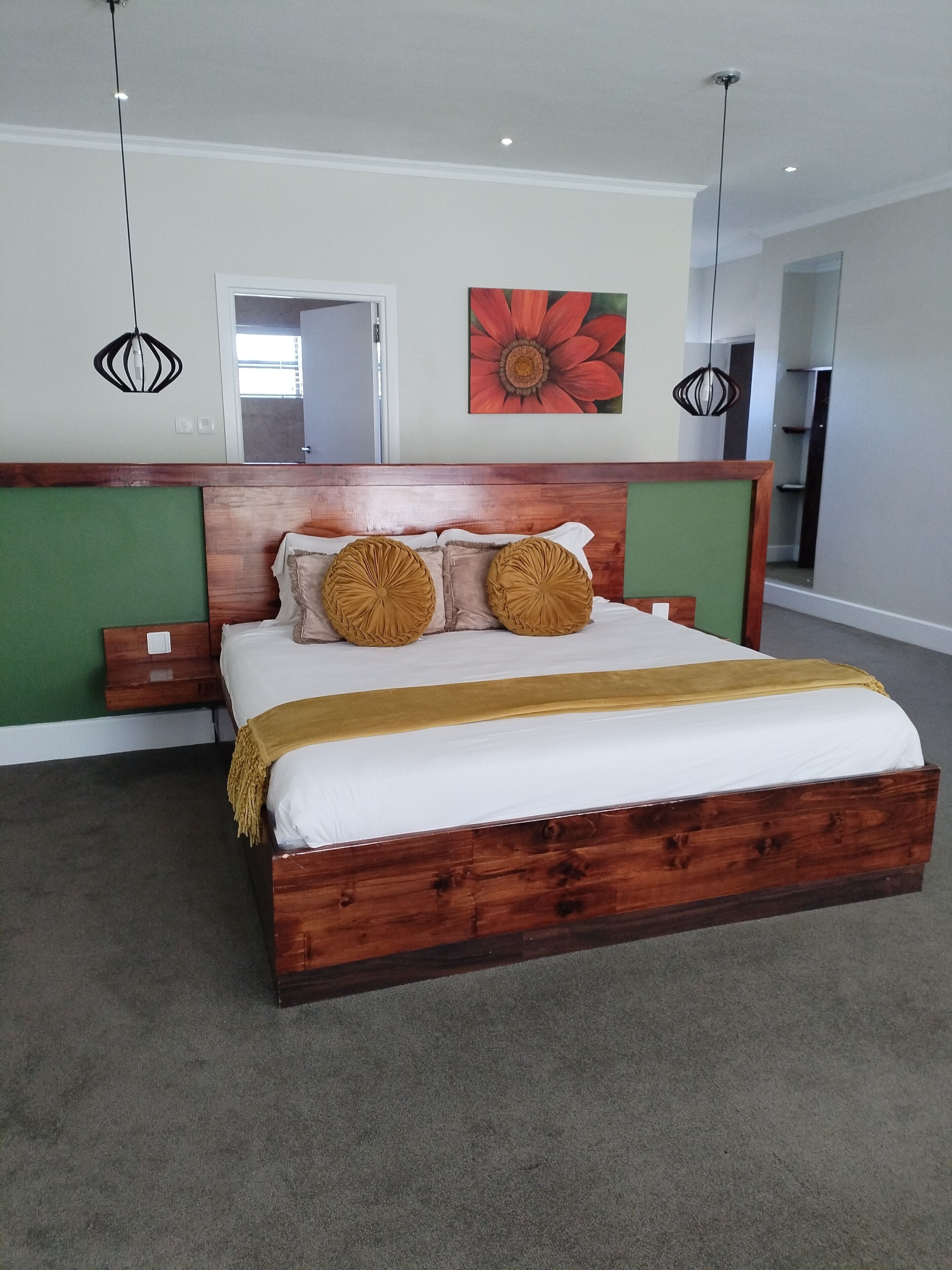 Quarto com cama de madeira, paredes com detalhes em verde, um espelho grande e um quadro com flores vermelhas.