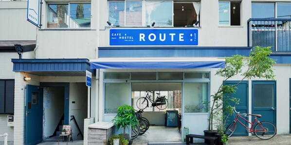 Albergue com toldo azul, bicicletas estacionadas na frente e placa indicando ser um albergue de rotas.