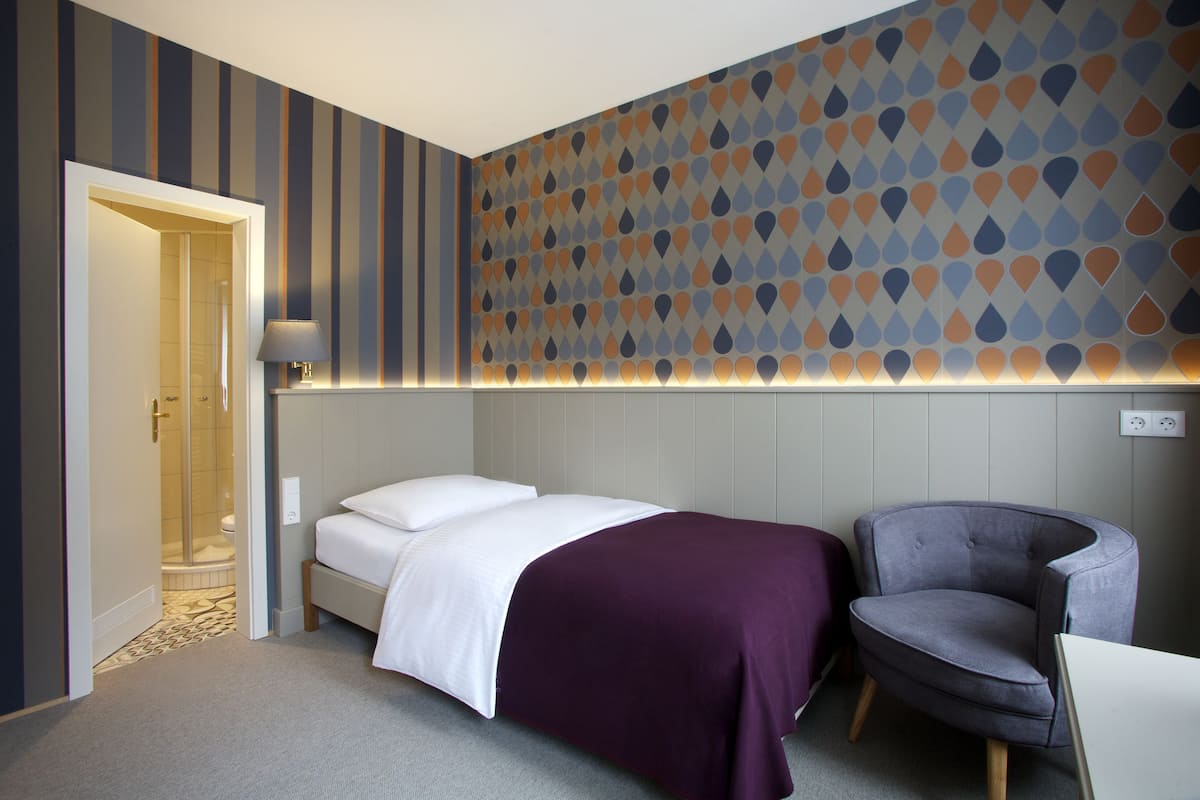 Quarto de hotel com cama, poltrona, chuveiro e parede estampada.