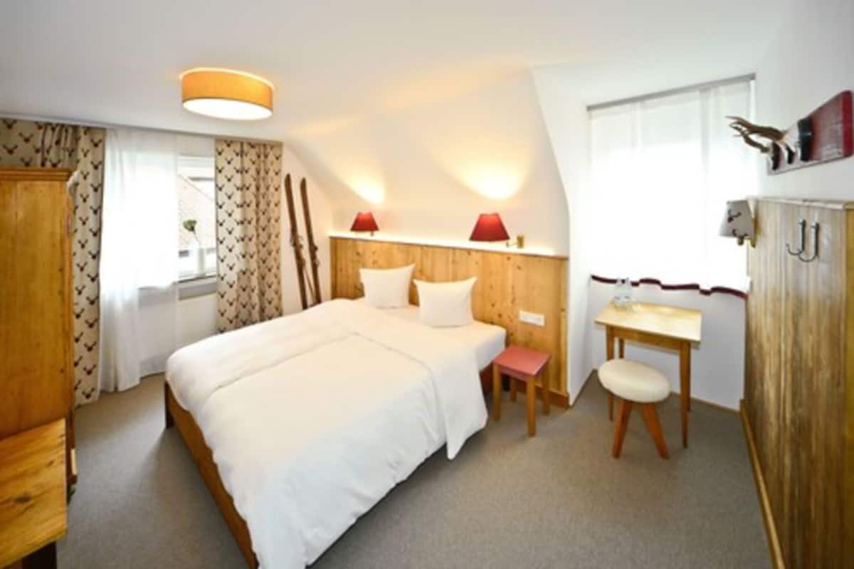 Quarto com uma cama grande, duas mesas de cabeceira com abajures, uma escrivaninha e um guarda-roupa.