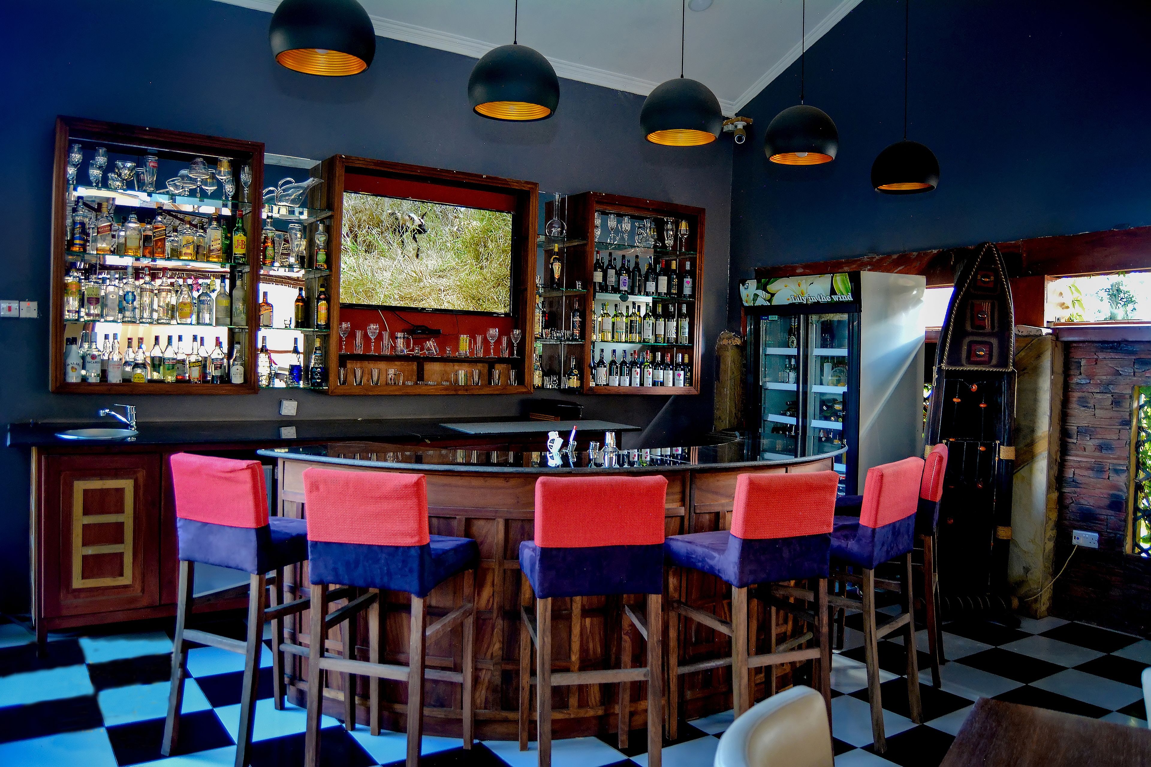 Uma área de bar com chão xadrez, balcão de madeira e vários bancos.