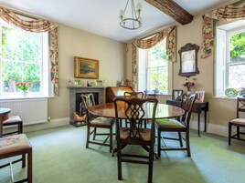 Uma sala de jantar com lareira, cortinas florais e uma mesa redonda com cadeiras.