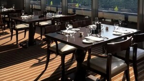Um restaurante com mesas preparadas para refeições, grandes janelas e vista para o exterior.