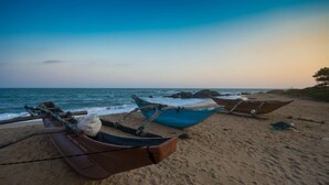 Uma praia com vários barcos atracados em troncos, areal e o oceano ao fundo.
