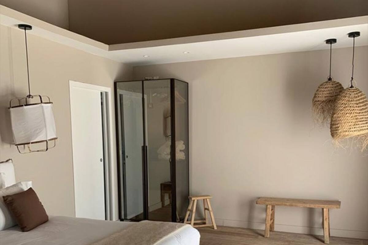 Quarto com uma cama grande, um banco de madeira, um guarda-roupa e luminárias pendentes.