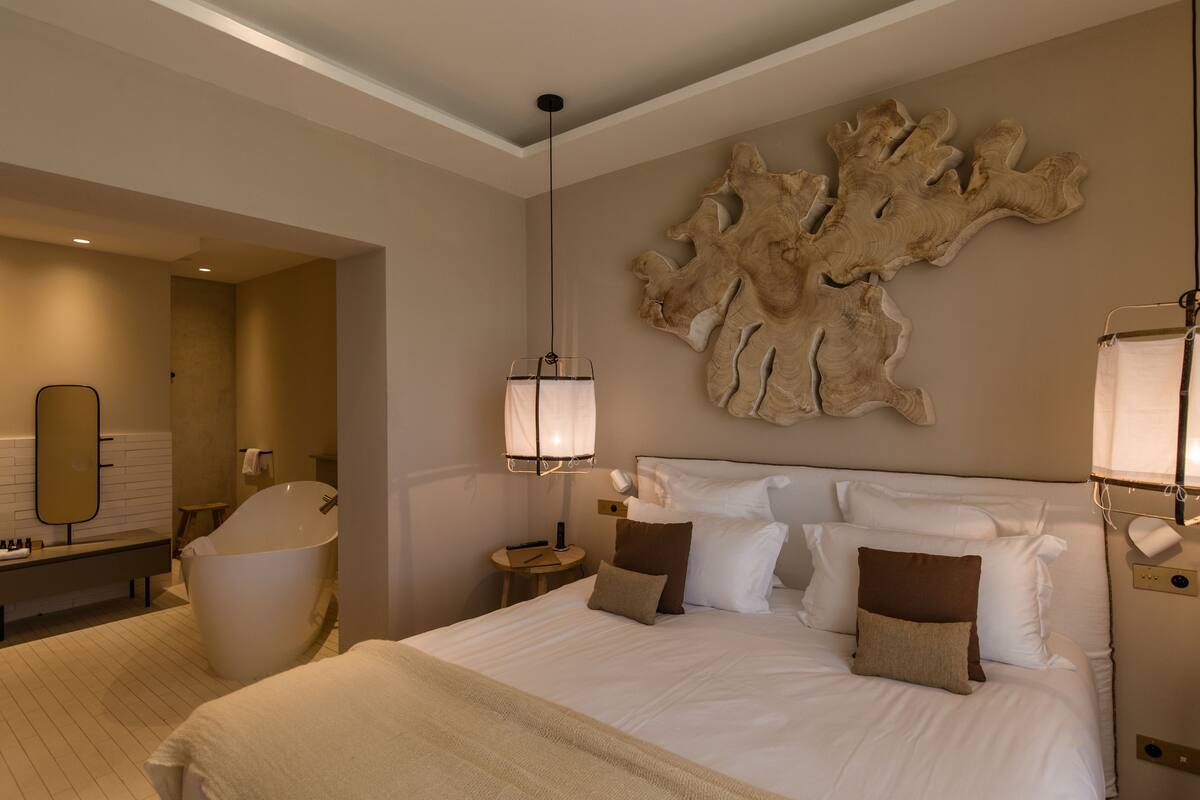 Quarto de hotel com uma cama grande, uma banheira, uma mesa redonda e um candeeiro fixado na parede.